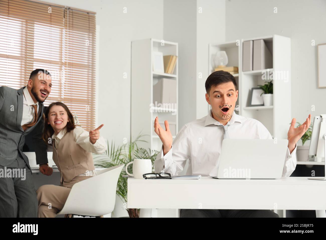 Shocked man with drawn mustache and his laughing colleagues in office ...