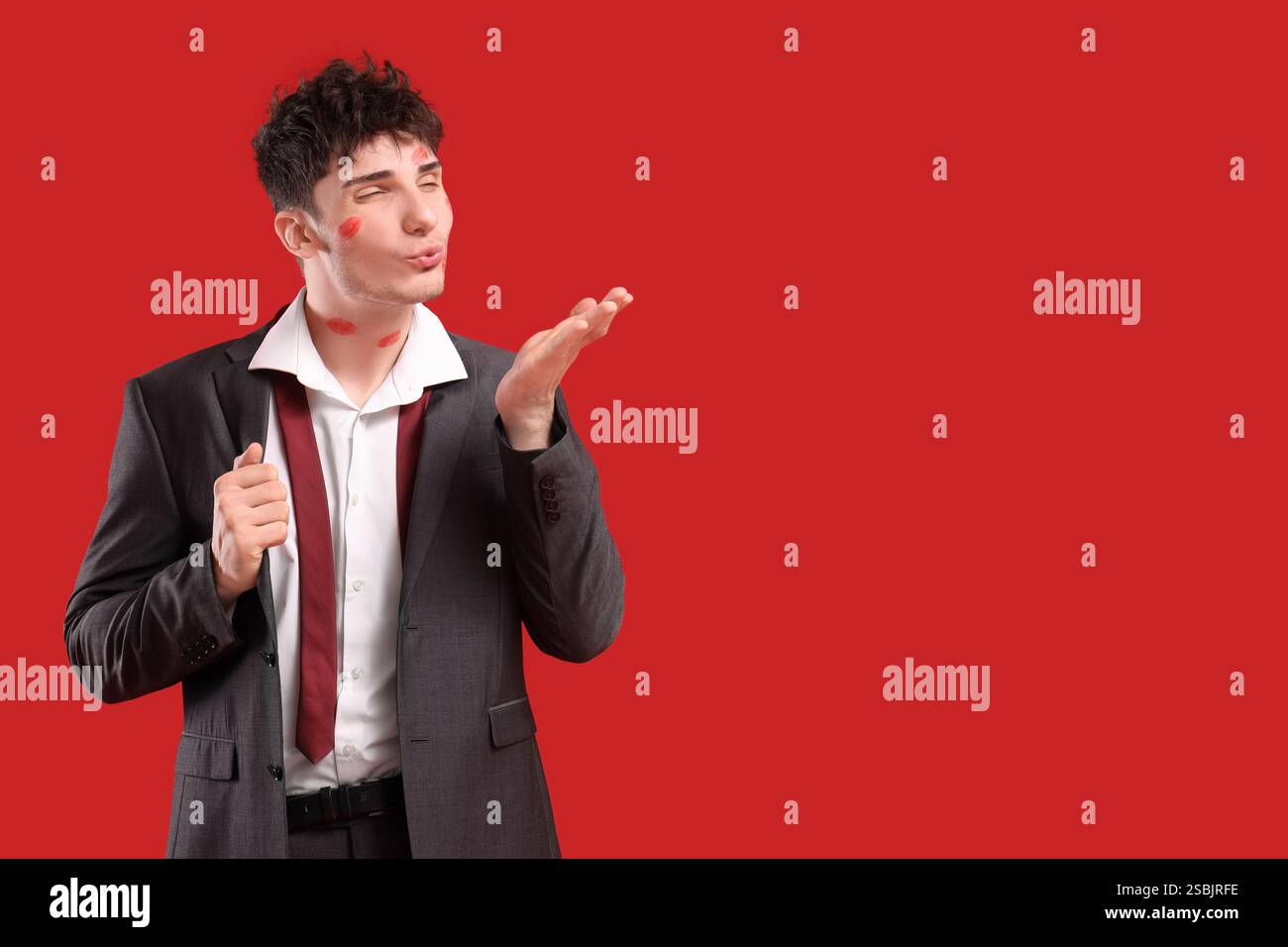 Handsome young man with lips marks on his face blowing kiss against red ...