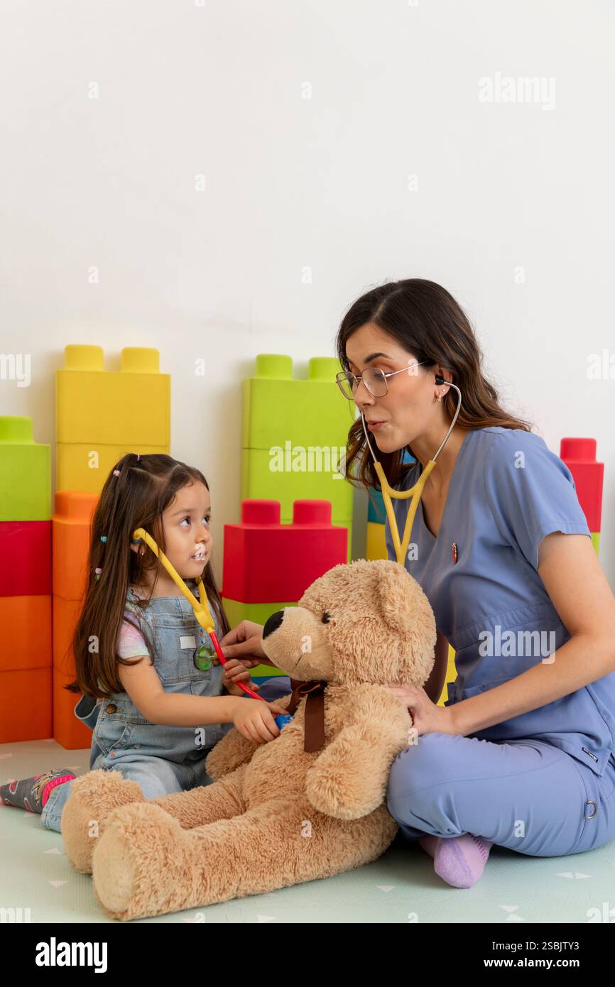 Pediatrician and girl playing doctor with teddy bear in clinic Stock ...