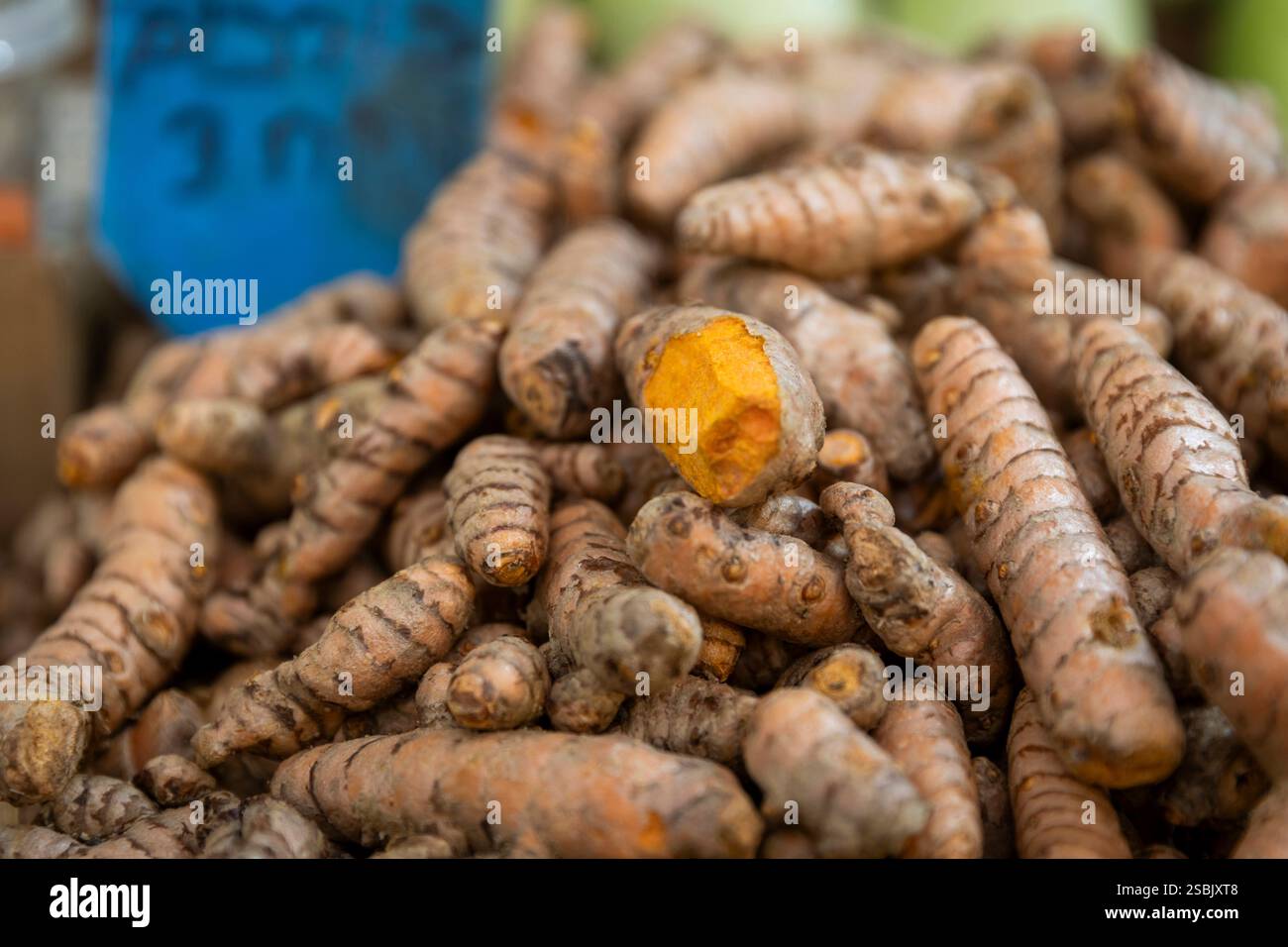 Turmeric roots stacked in a heap for sale at a stall. One is sliced in ...