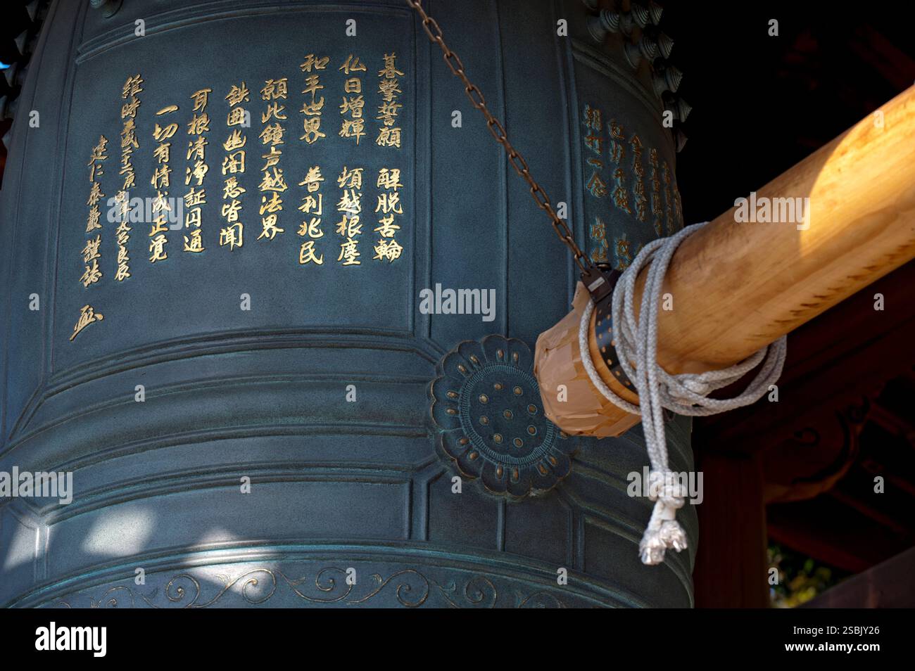 Large bronze bell with gold script on side and horizontal wooden pole ...