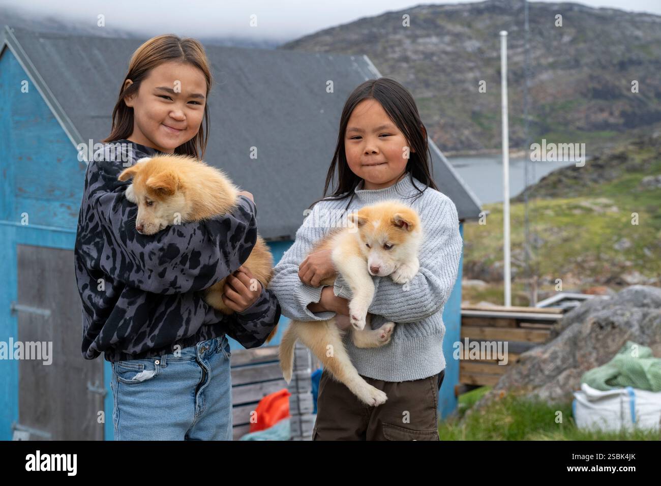 Two Little Inuit girls hold fluffy puppies while smiling in the ...