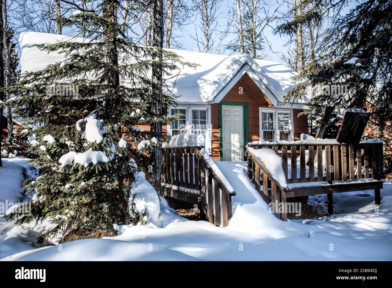 A cabin with a porch and steps covered in snow. The porch has a bench ...