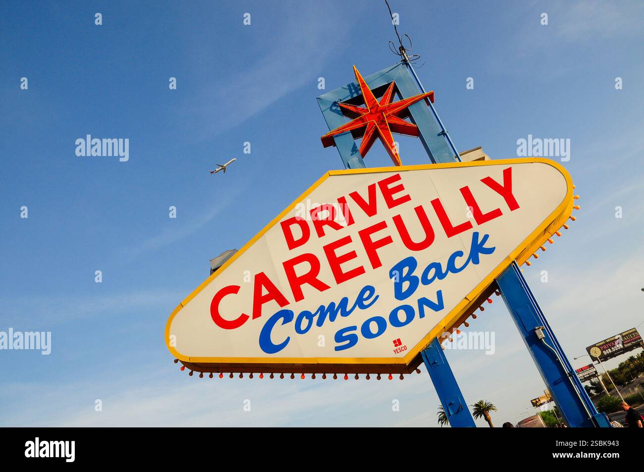Iconic retro sign under a clear blue sky with an airplane soaring above ...