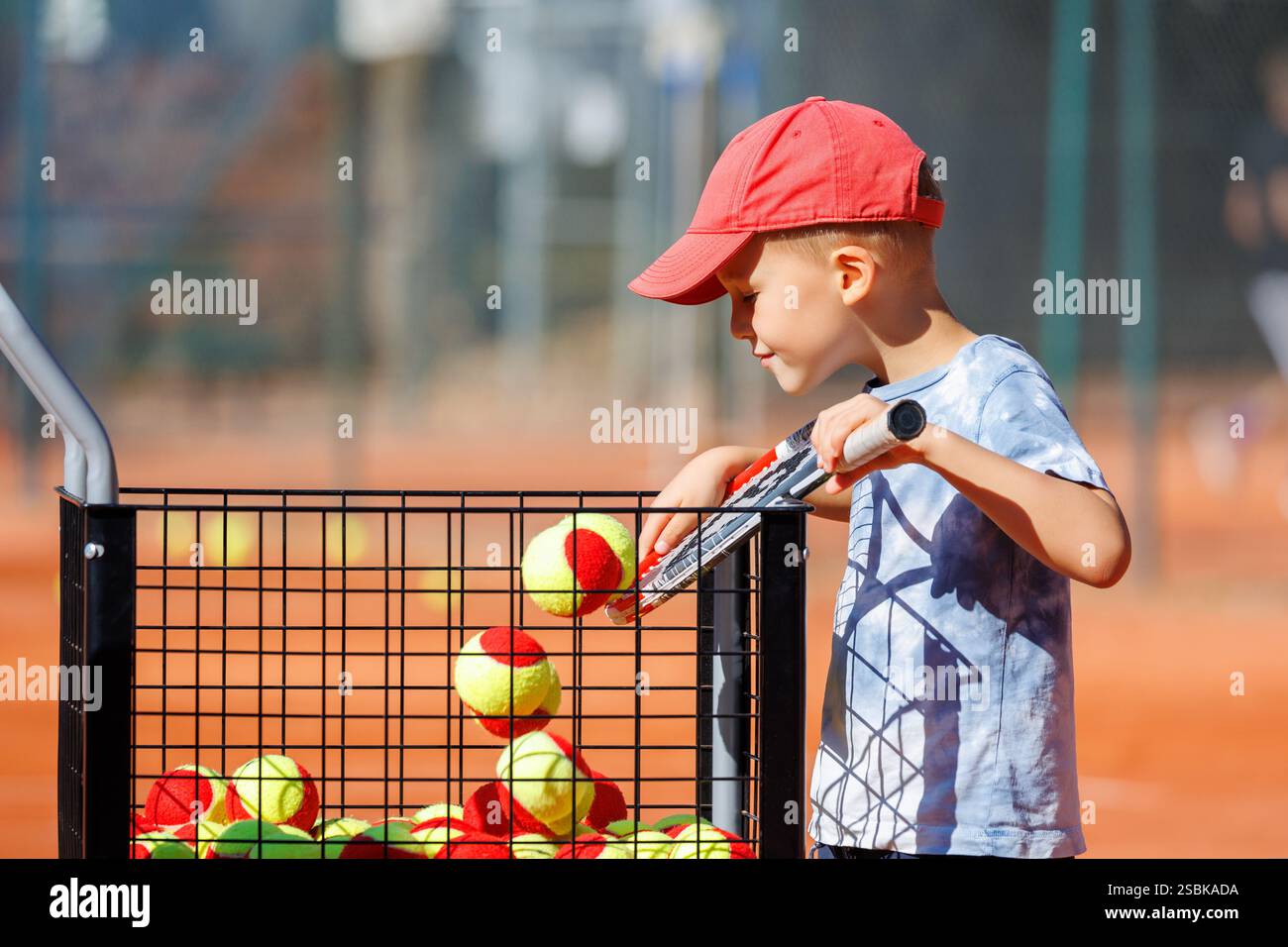 Cute little happy kid boy enjoy collecting balls in basket cart sign ...