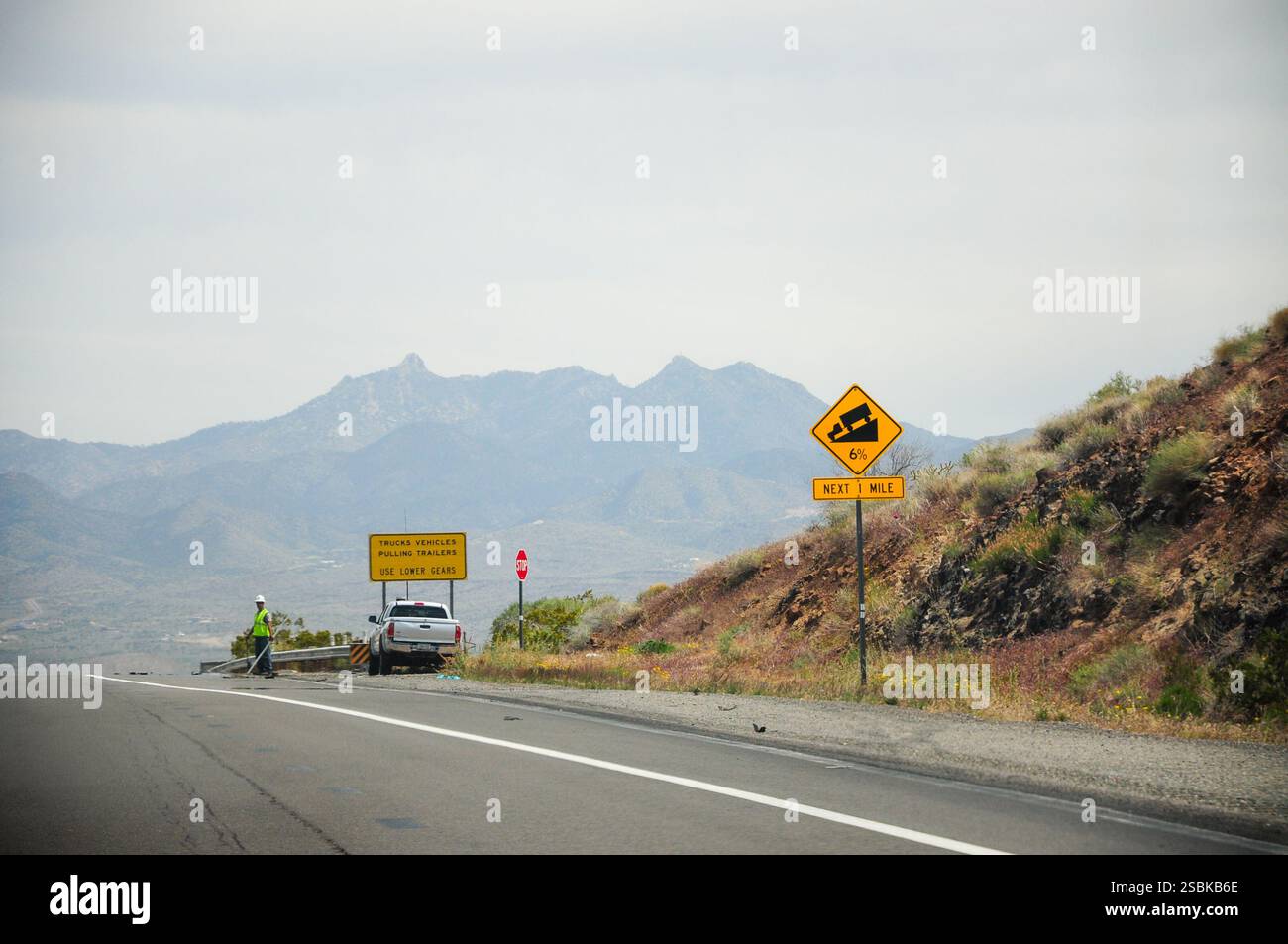 Scenic mountain road with vehicle and steep incline warning on cloudy ...