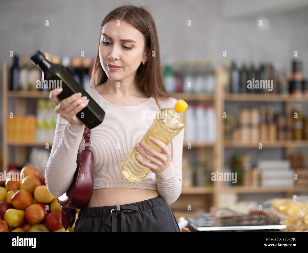Girl buyer looks thoughtfully and indecisively at bottles of vegetable ...