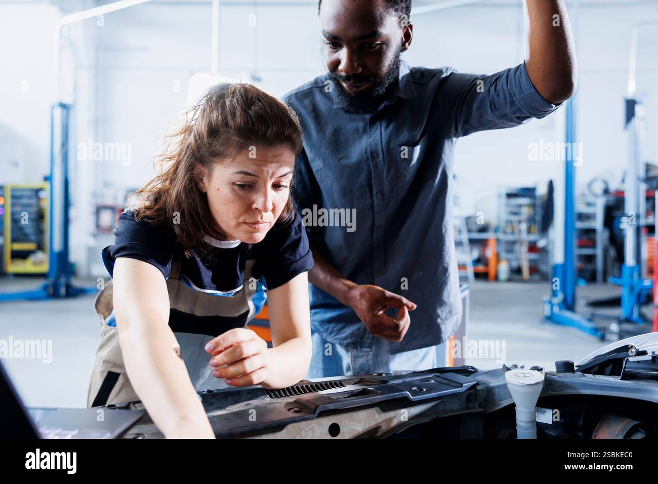 Adept mechanic helping client with car checkup in auto repair shop ...