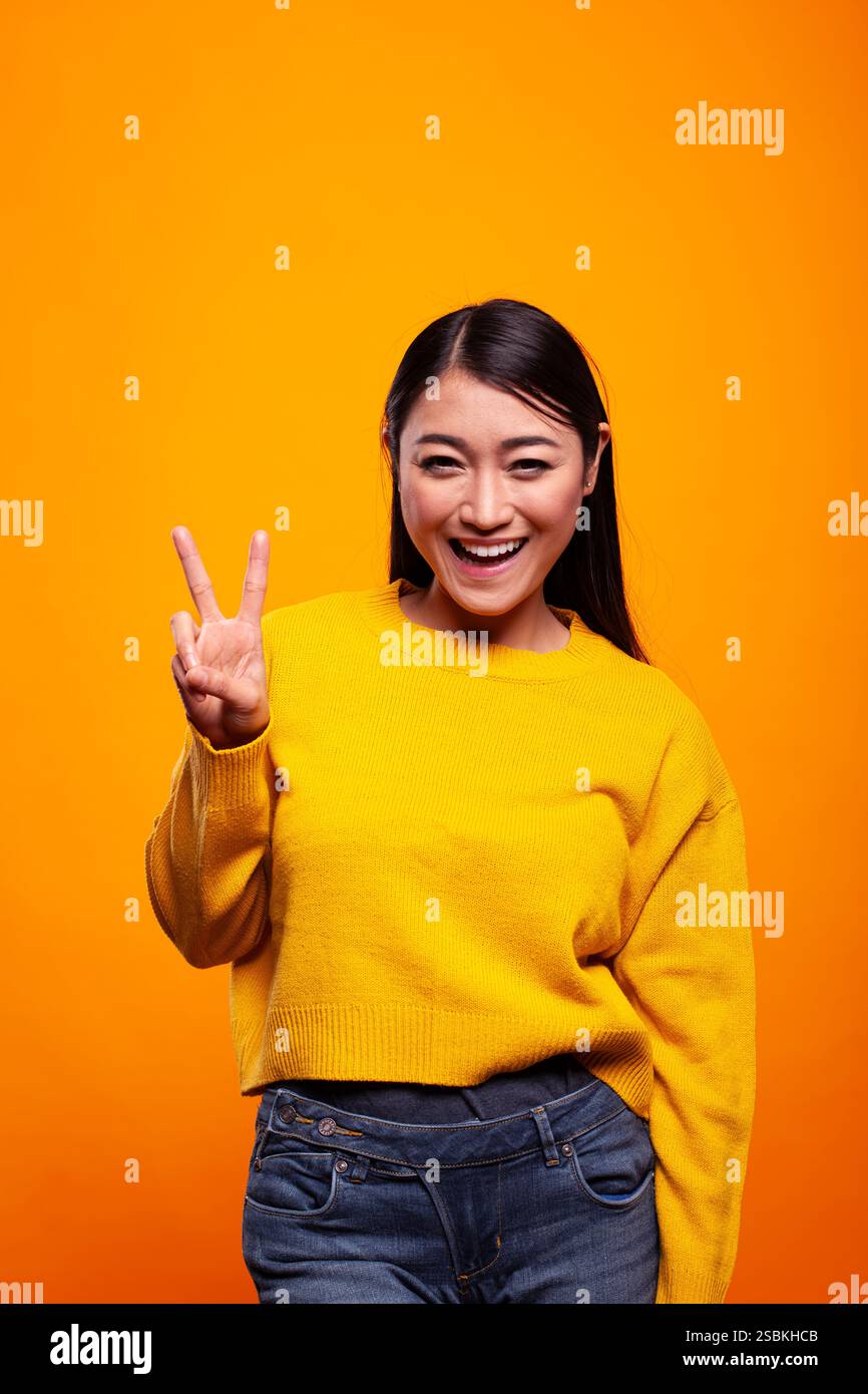 Asian woman in a yellow sweater standing joyfully and flashing the ...