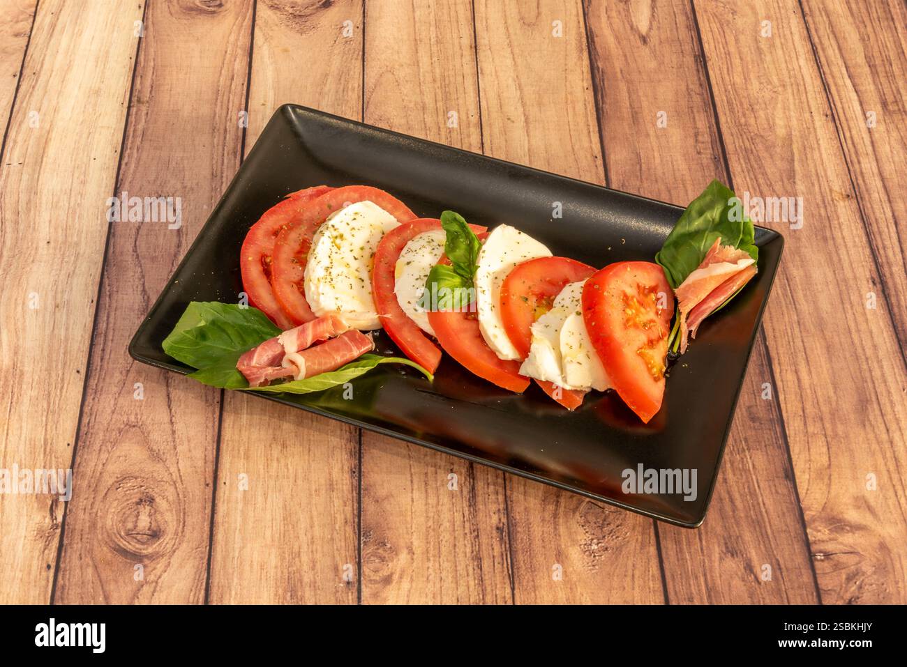A black tray with a caprese salad with some ham and basil Stock Photo ...