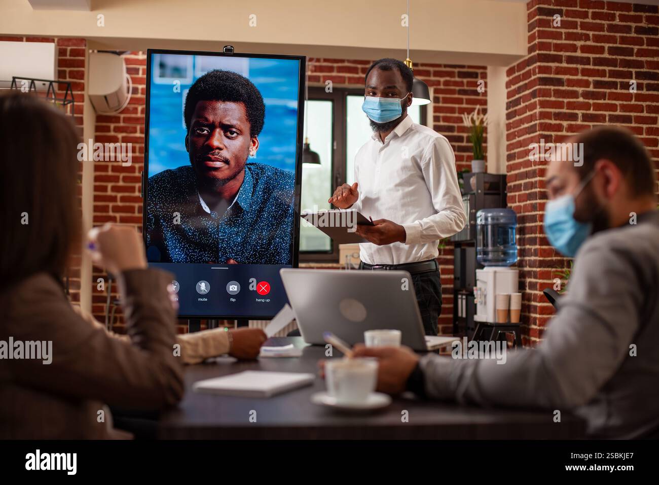 Face masked black man presents updates to remote client on video call ...
