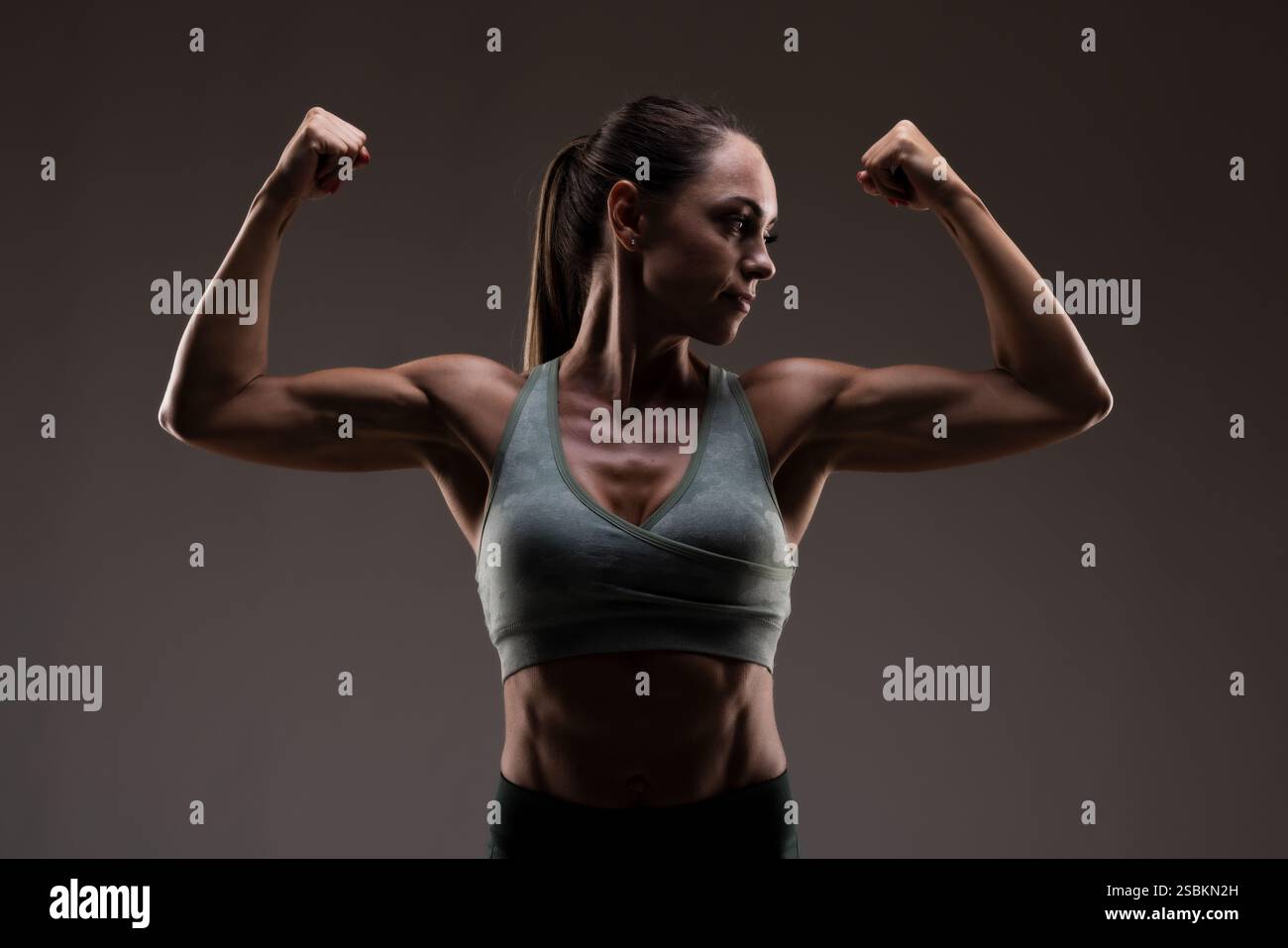 A strong and confident woman flexing her muscular arms in a fitness ...