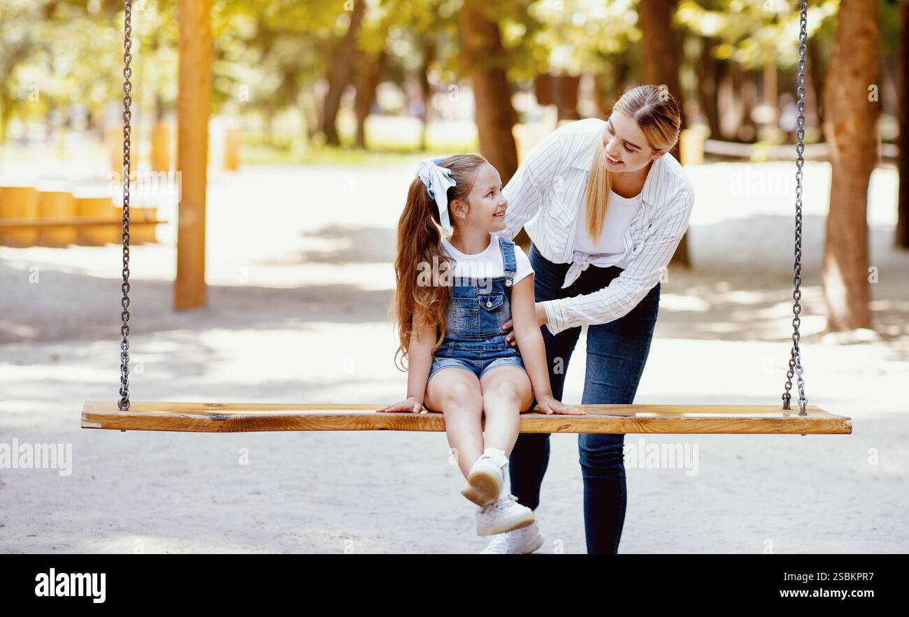 Mother Pushing Daughter On Swings Spending Time Together On Playground Stock Photo - Alamy