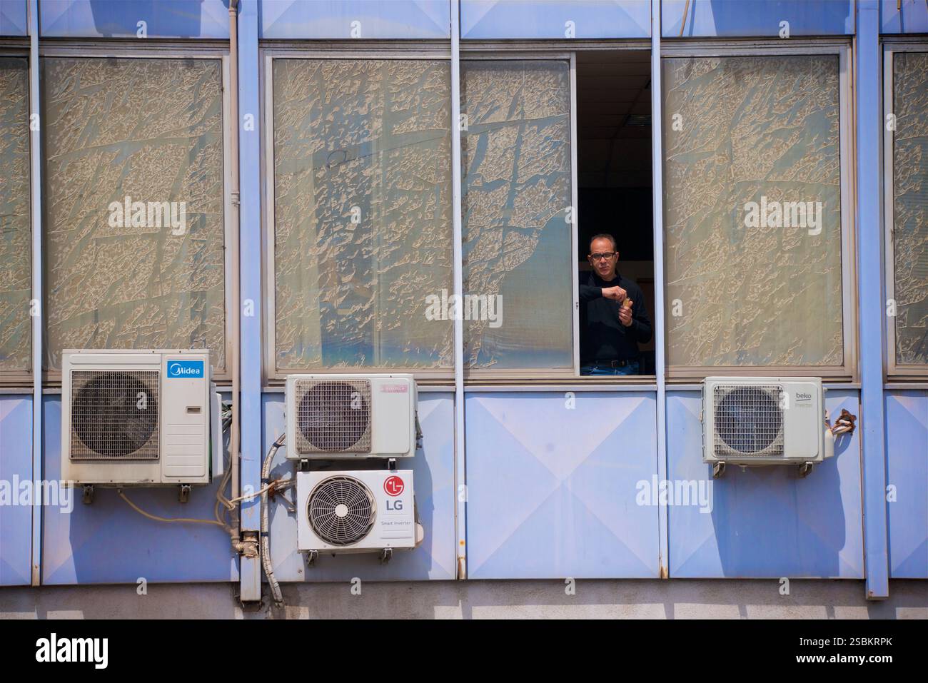 Man looking out of a window in a modern building with air conditioning ...