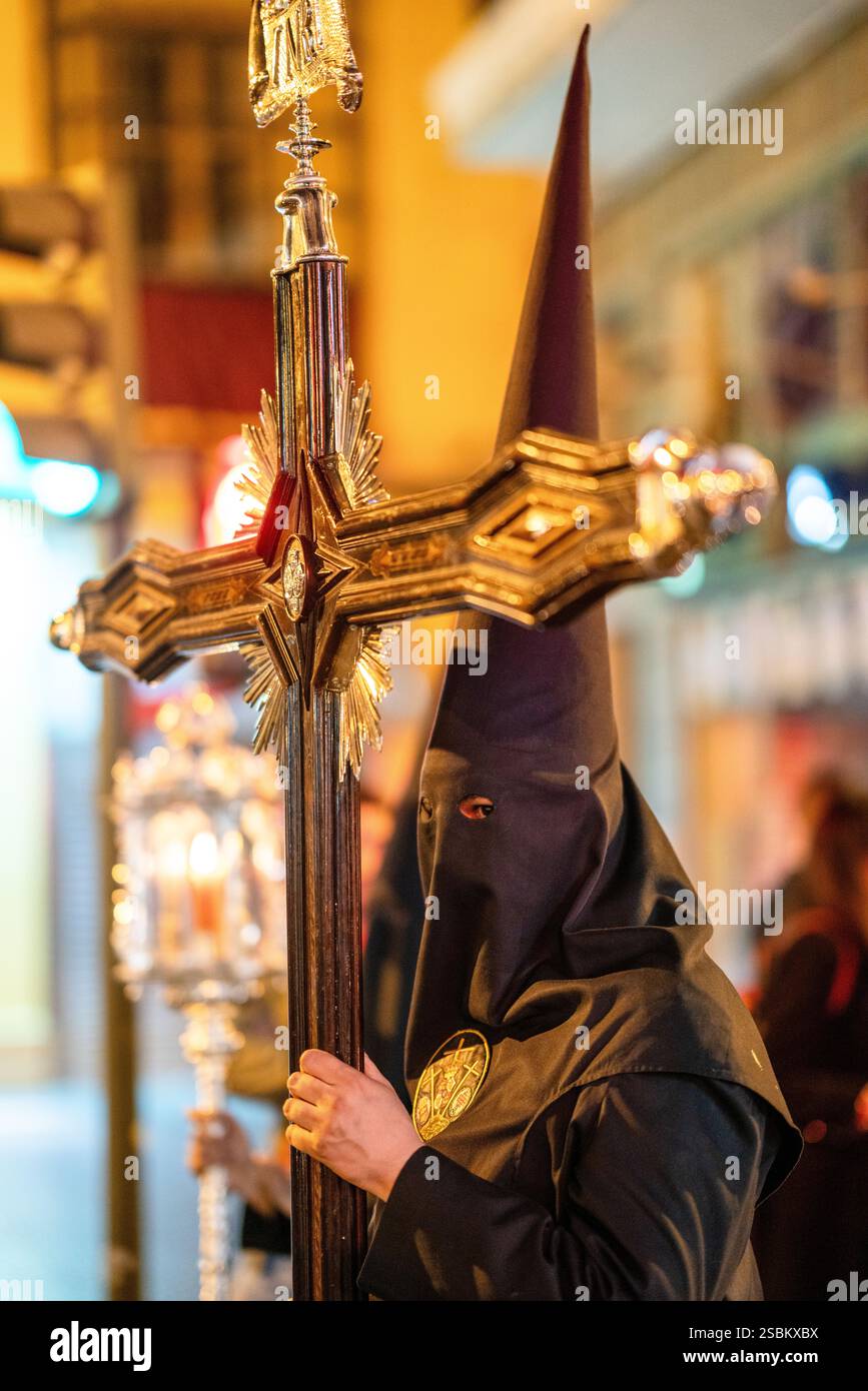 A hooded figure carries an ornamental cross during a Holy Week ...