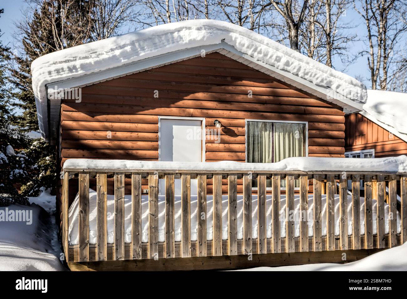 A log cabin with a snow covered roof. The cabin has a porch with a ...