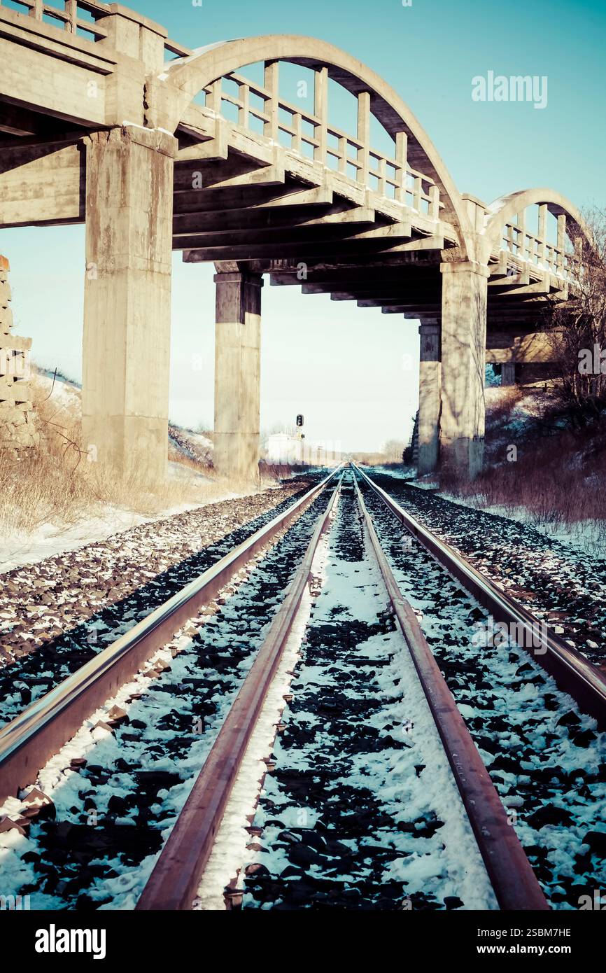 Bridge with train tracks underneath it. The tracks are covered in snow ...