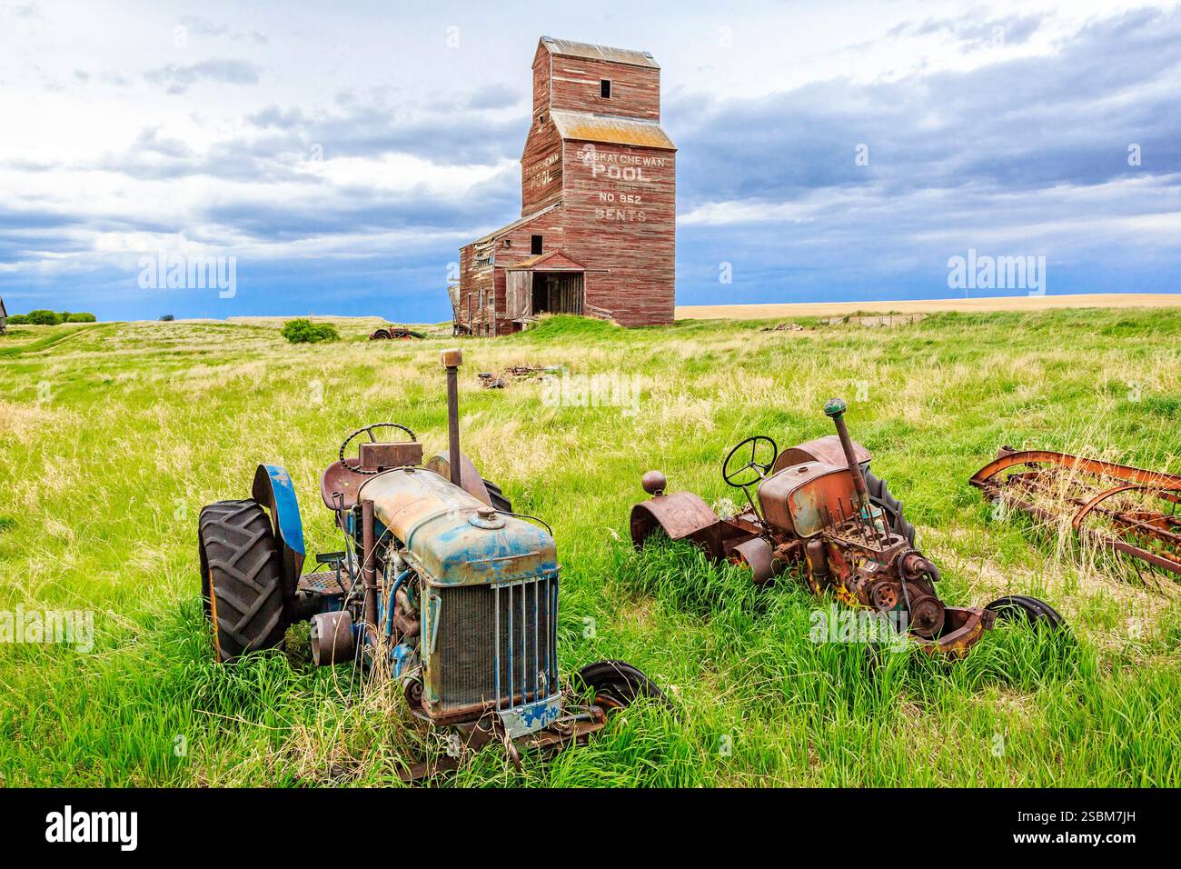 Two old tractors are parked in a grassy field next to a building. The ...