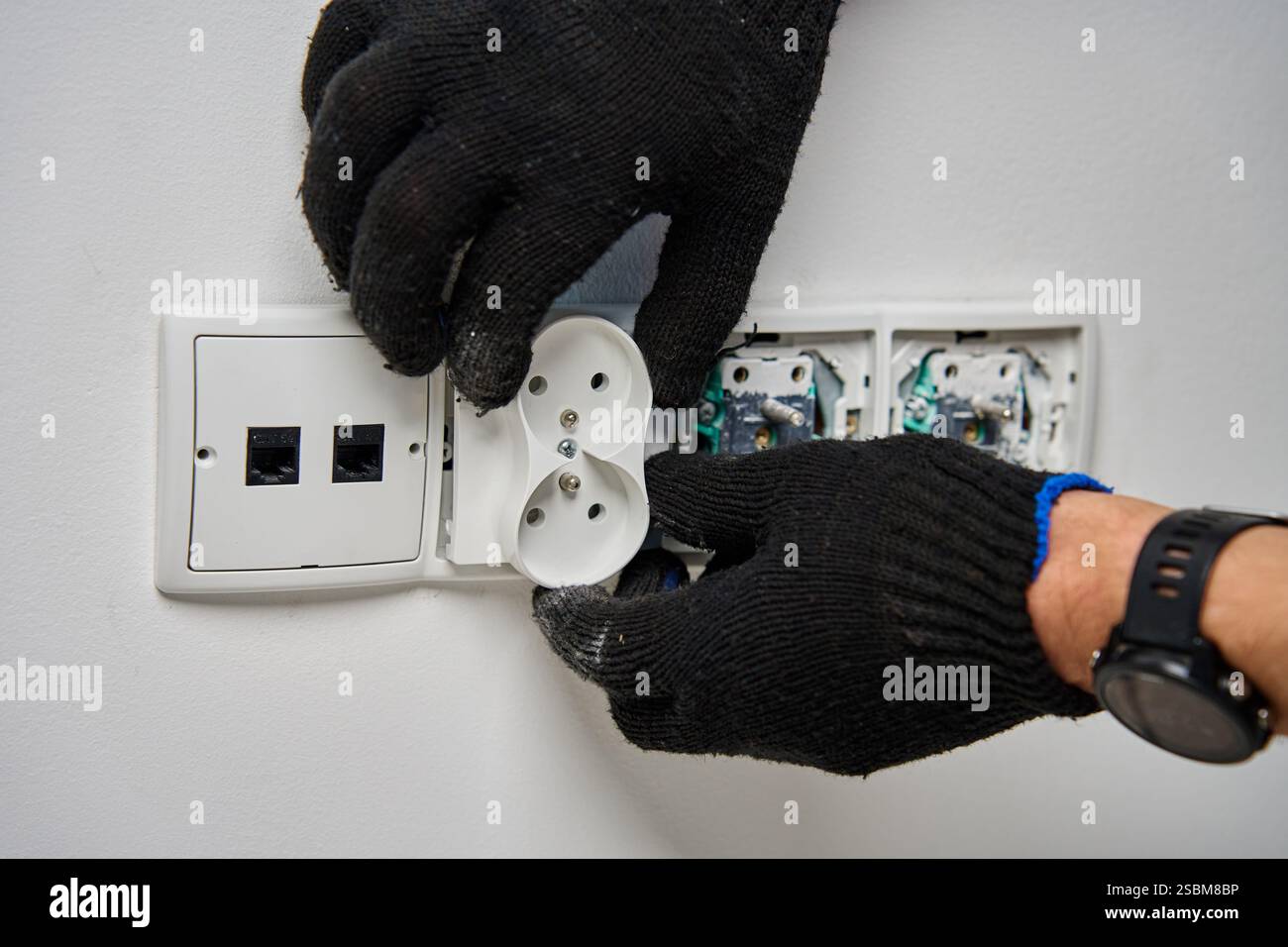 Close-up of an electrician wearing black gloves installing power socket ...