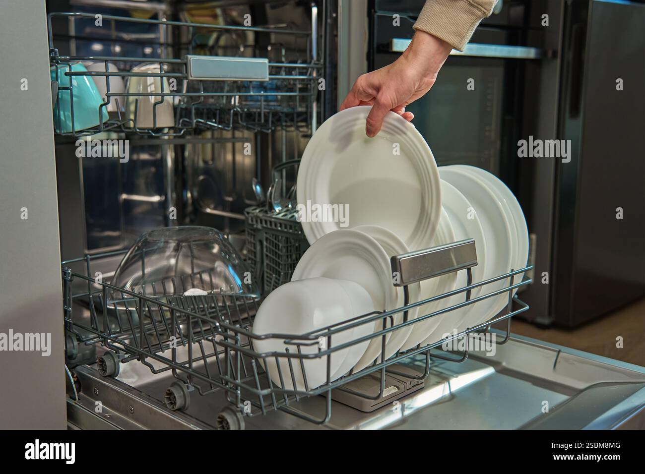 Woman unloading clean white plates from the bottom rack of dishwasher ...