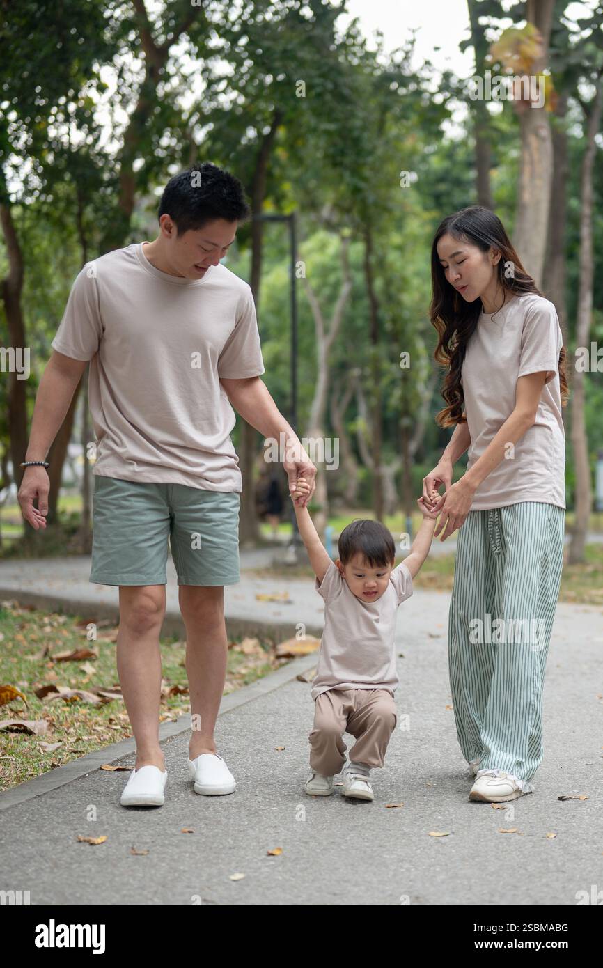 Caring and happy Asian parents hold their son's hand while walking in a ...