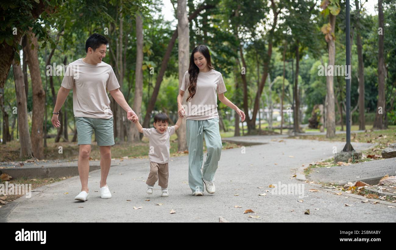 Caring and happy Asian parents hold their son's hand while walking in a ...