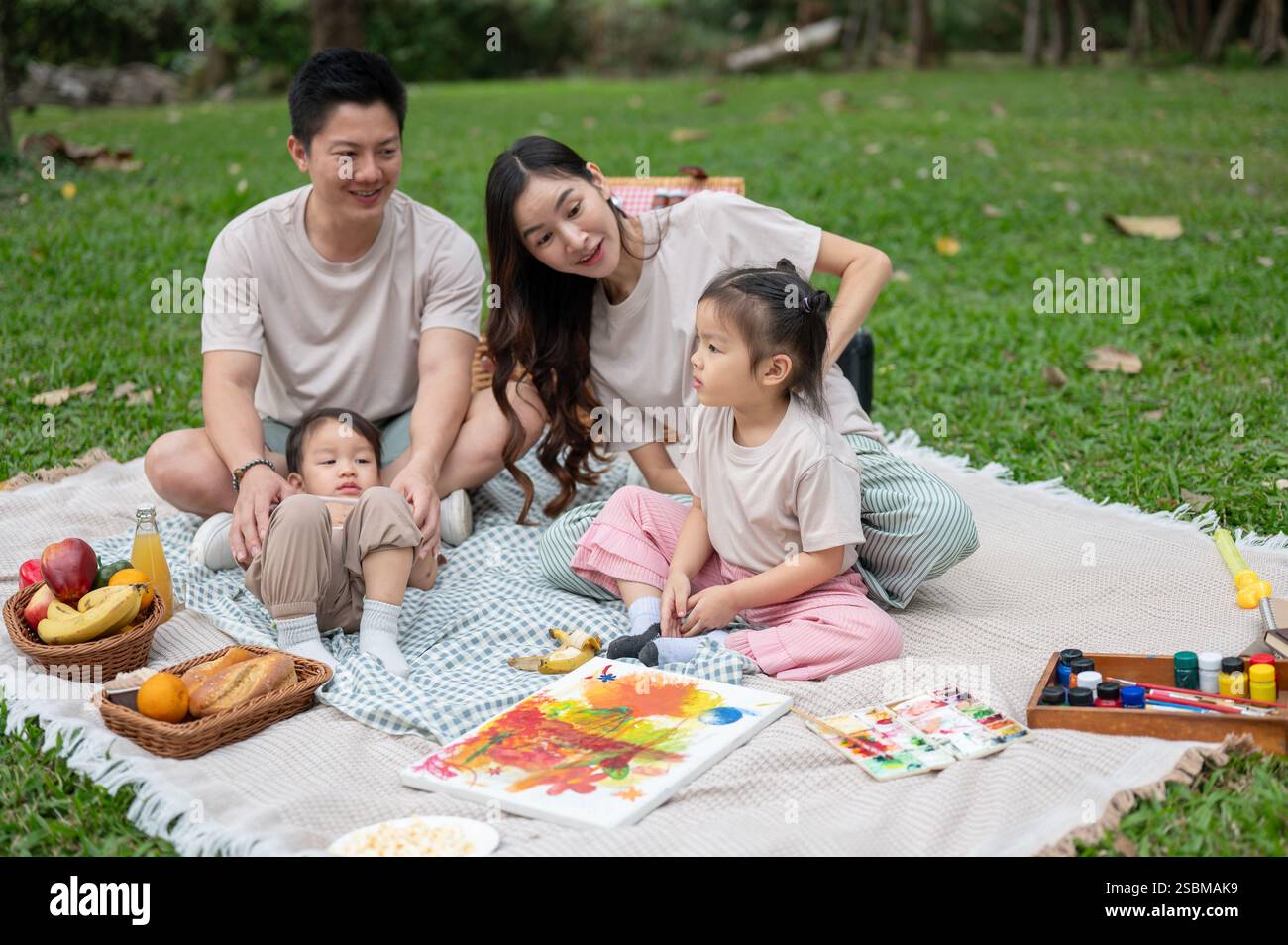 Caring Asian parents take their kids on a picnic in a public park ...