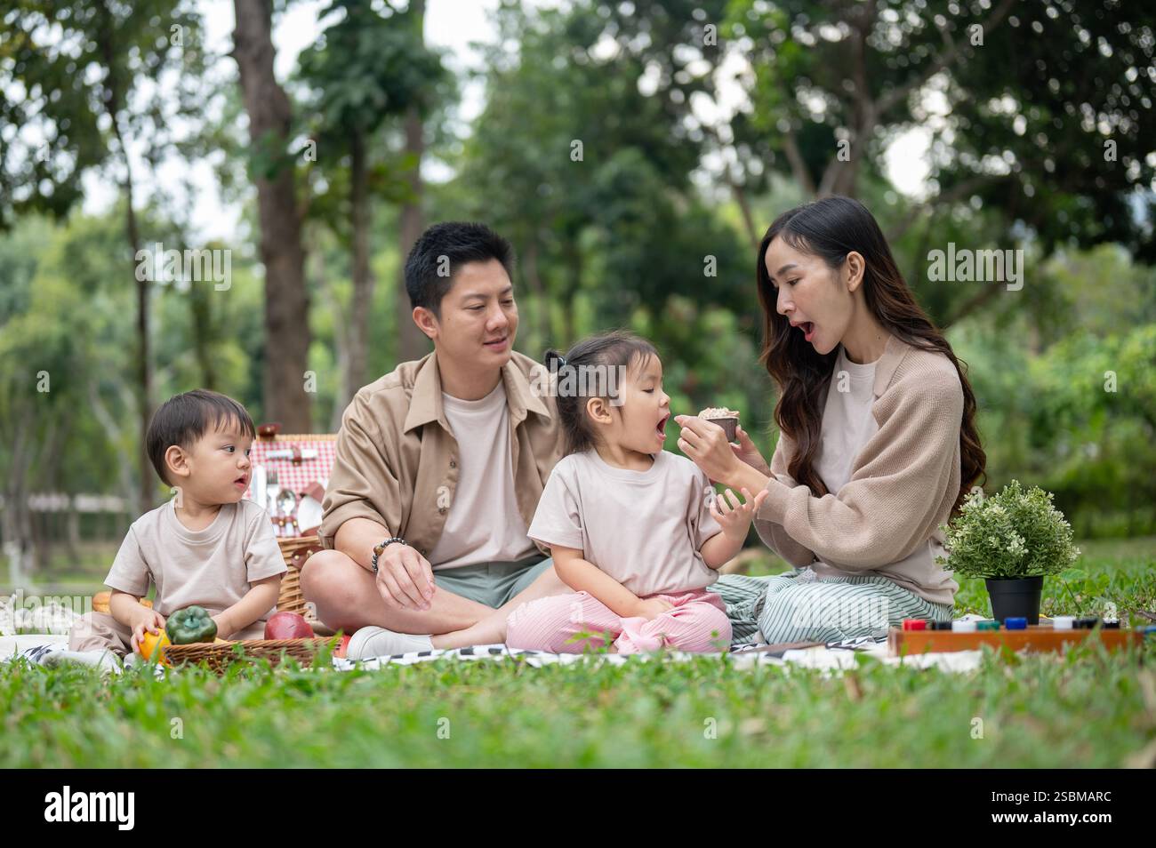 A joyful, happy Asian family picnics in a green public park, sitting on ...