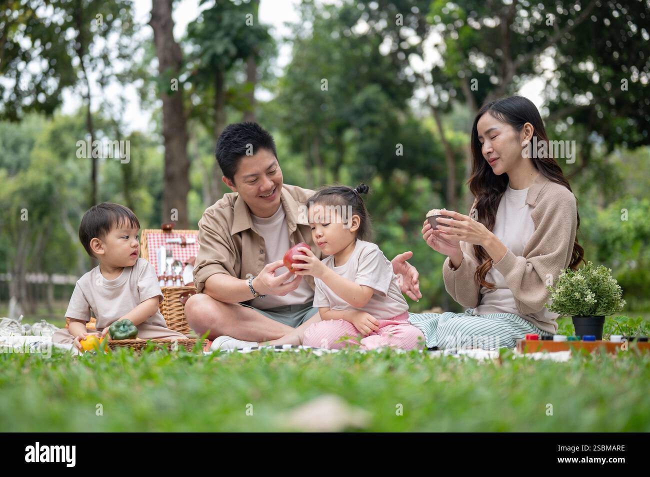 A joyful, happy Asian family picnics in a green public park, sitting on ...