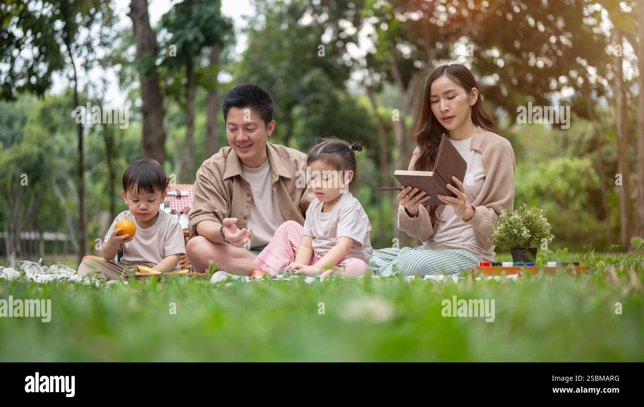 A joyful, happy Asian family picnics in a green public park, sitting on ...
