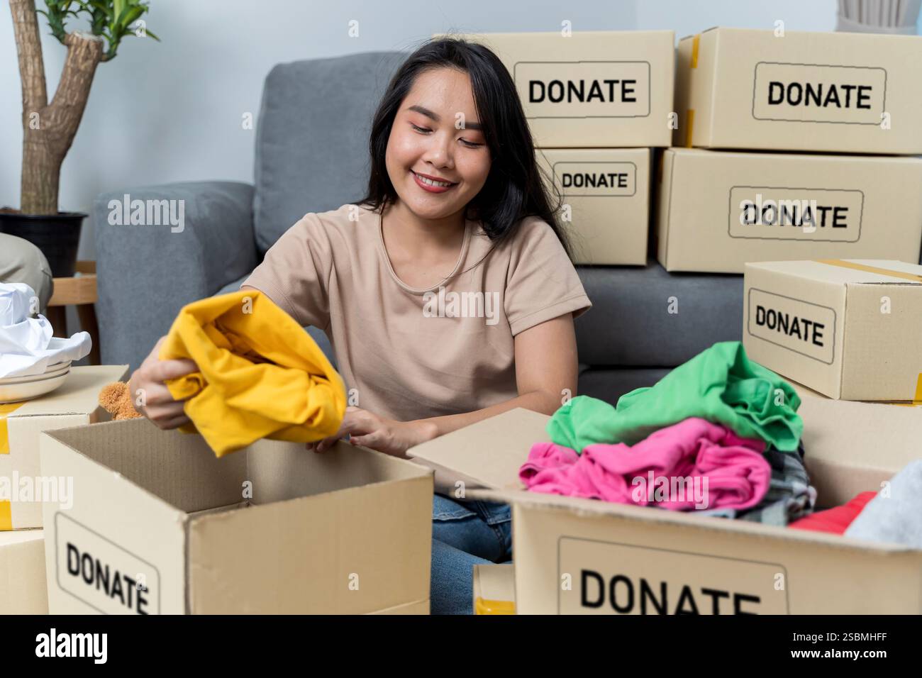 Woman sorting clothes while packing donation boxes for charity. Volunteer with donation box with ...