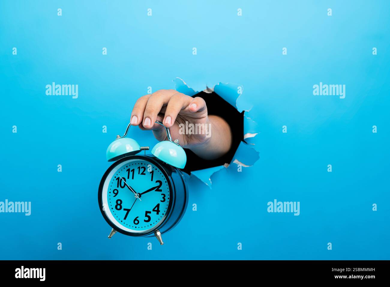 Human hand holding alarm clock through ripped paper. Mockup or Copy ...