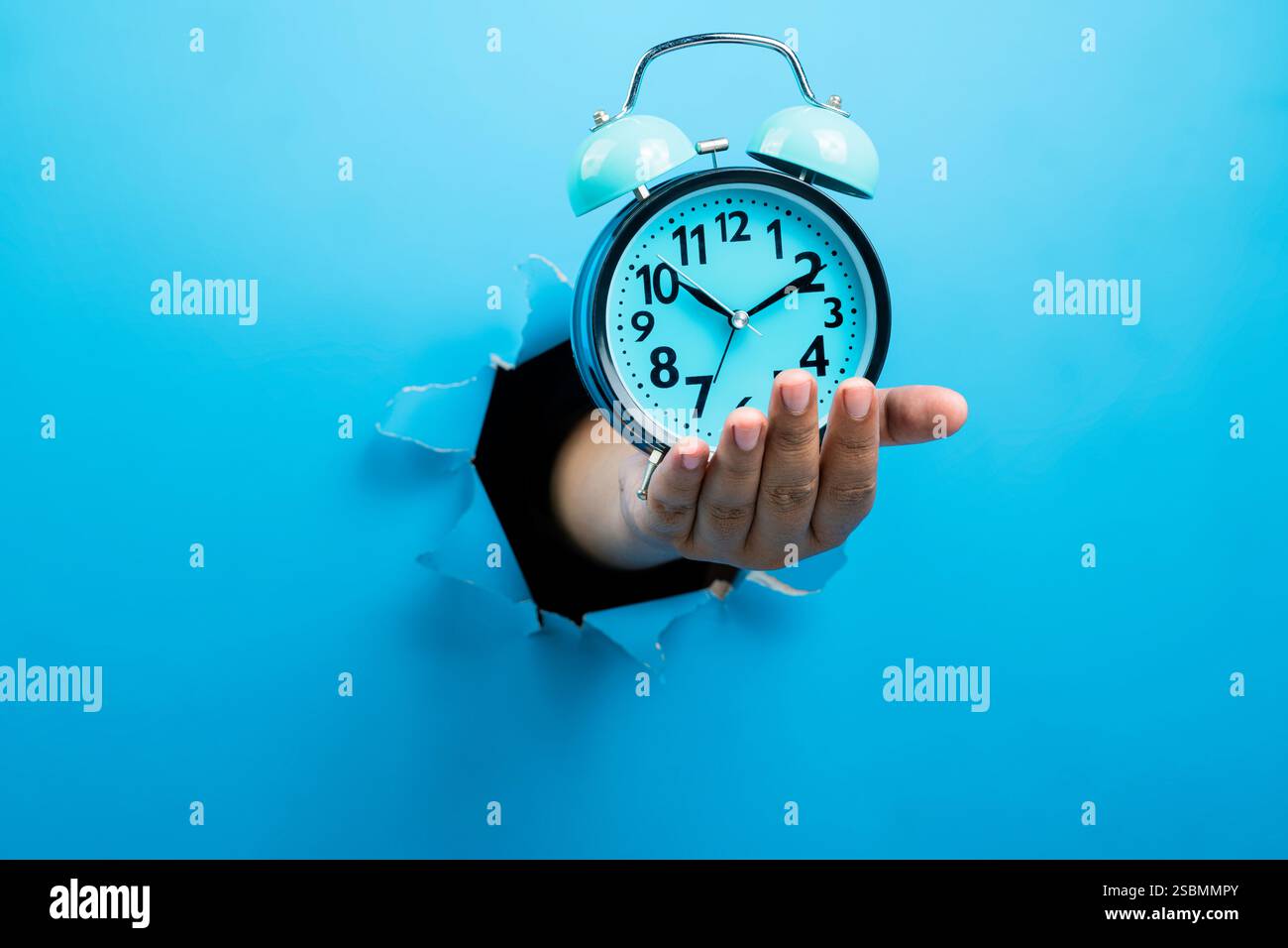 Human hand holding alarm clock through ripped paper. Mockup or Copy ...