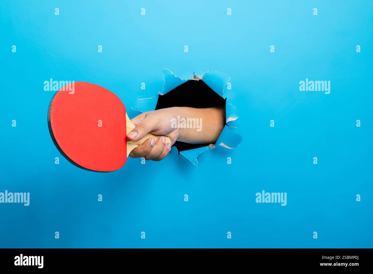 Human hand holding table tennis paddle through ripped paper. Mockup or ...