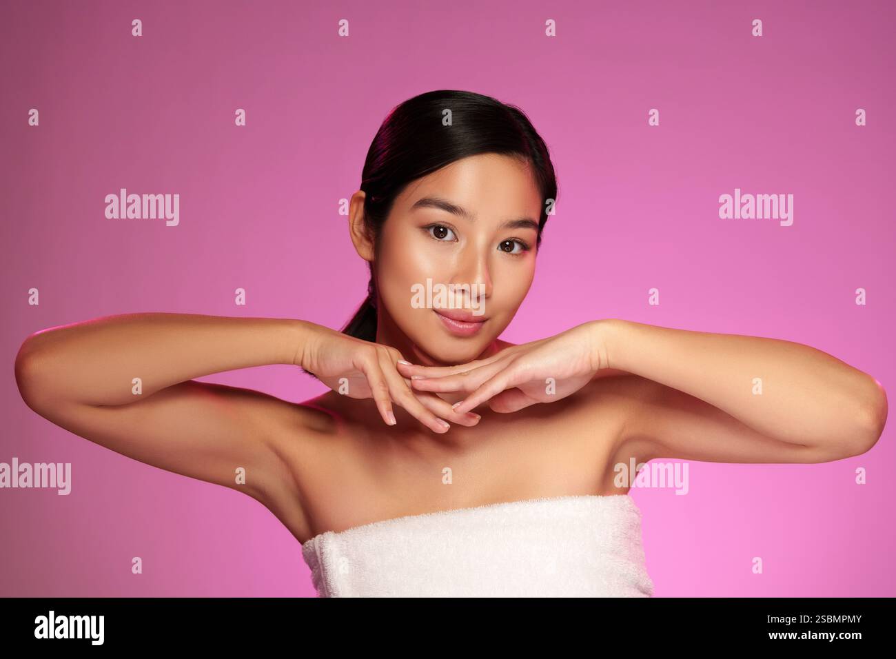 Confident young woman posing with hands under chin in front of pink ...
