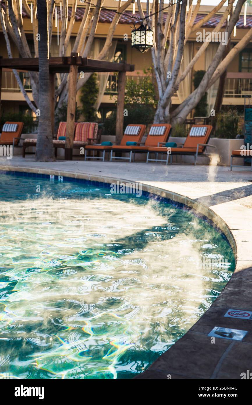 A pool with a fog machine on the side. There are several lounge chairs ...