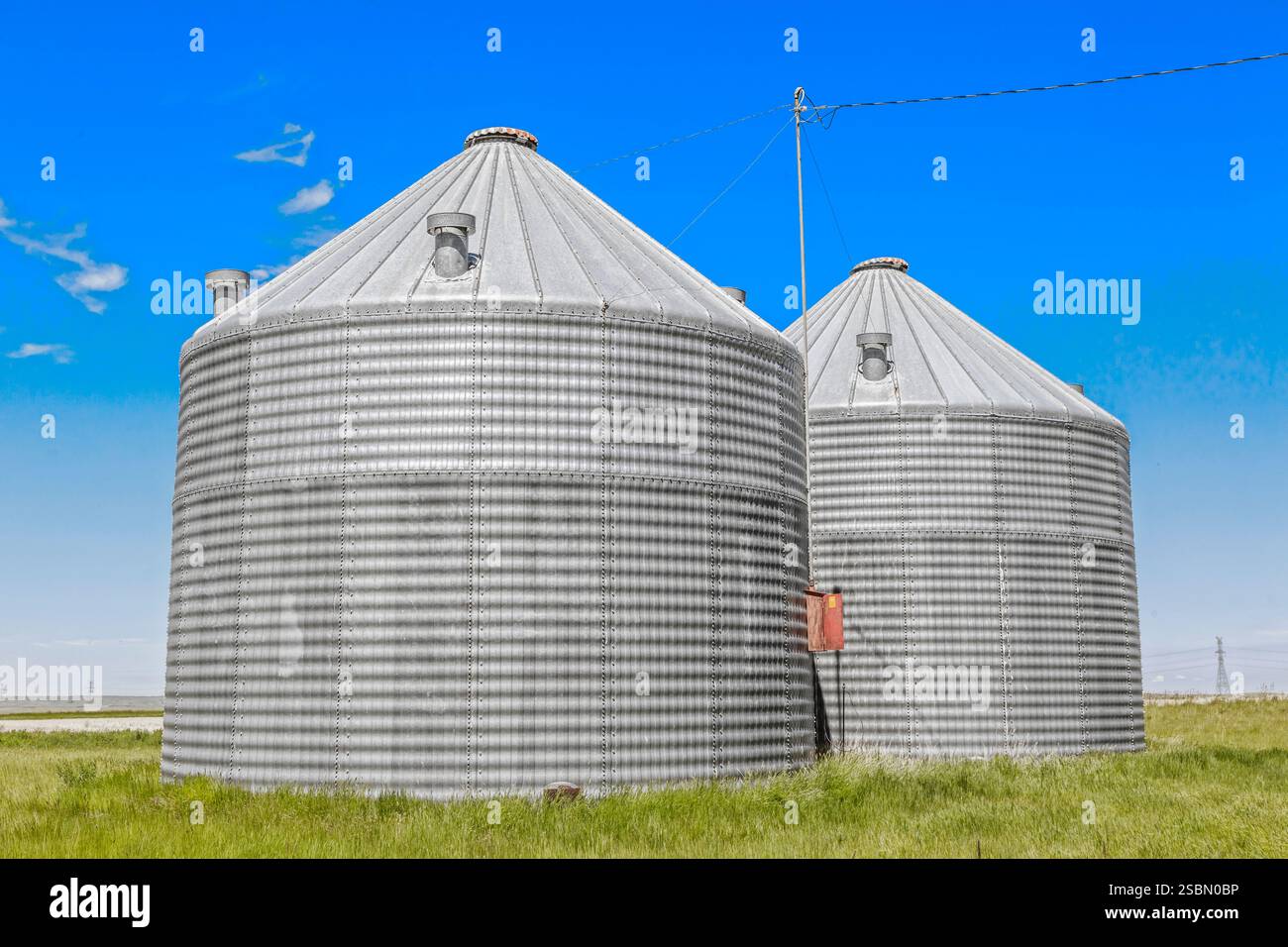 Two large metal silos are sitting in a field. One of the silos is empty ...