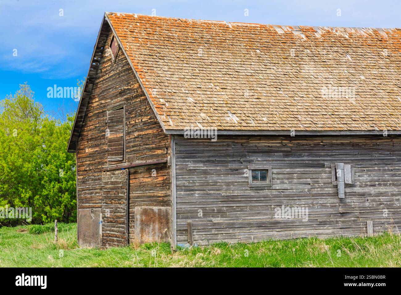 Large, old barn with a slanted roof. The roof is made of wood shingles ...