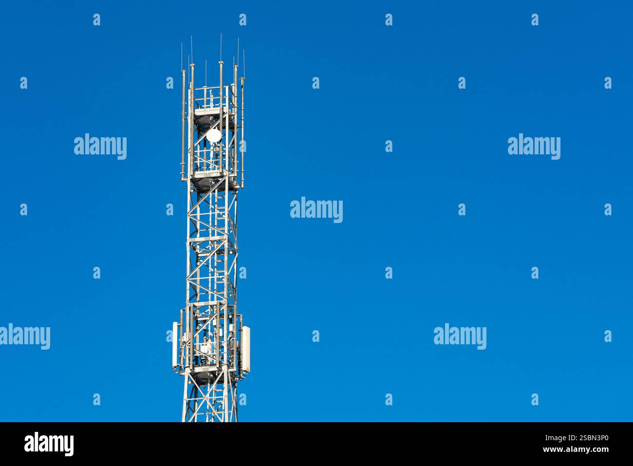 A tall metal structure rises into a clear blue sky, featuring multiple antennas and equipment ...