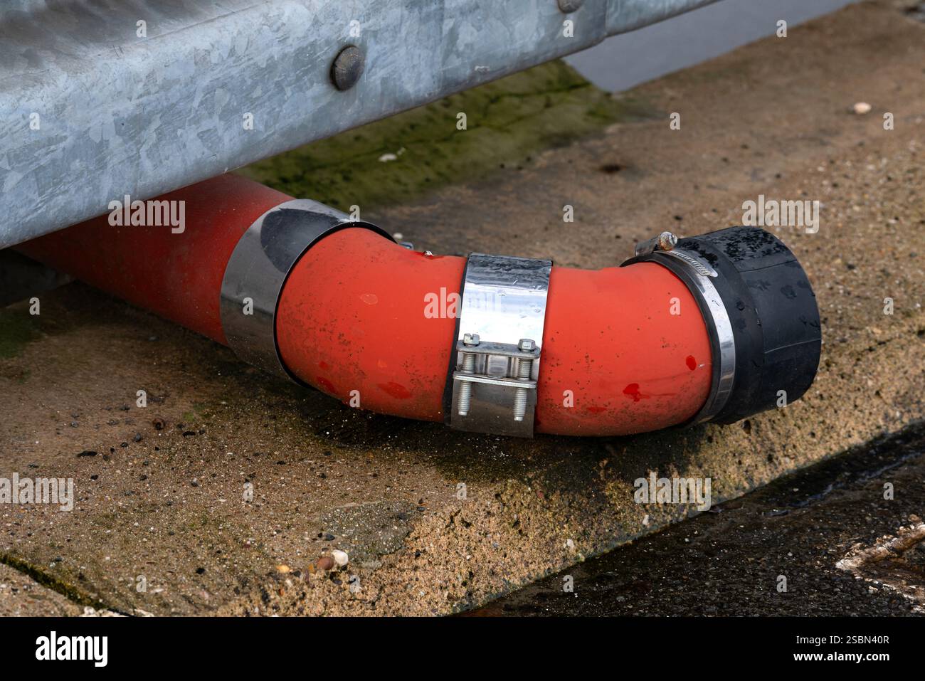 A red drainage pipe is seen bending as it connects to the concrete ...