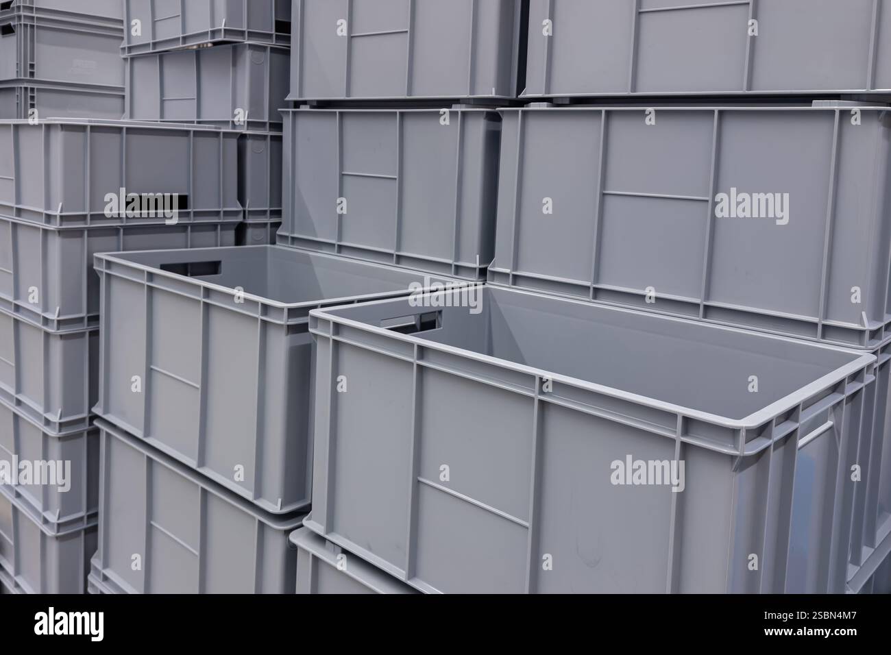 Sturdy grey storage containers are stacked neatly in a warehouse. Each ...