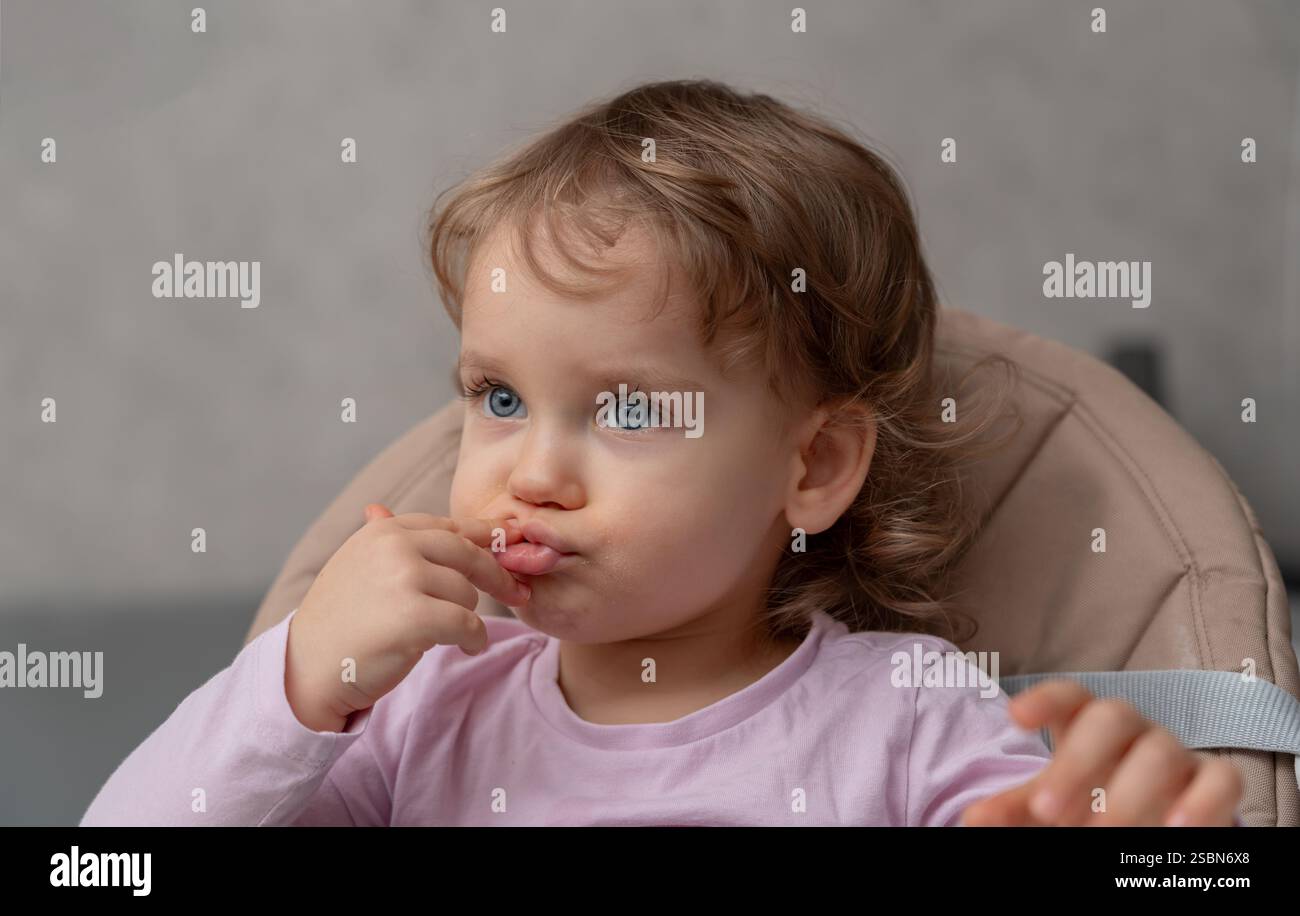 A toddler making a funny face while chewing food at the table in a cozy ...
