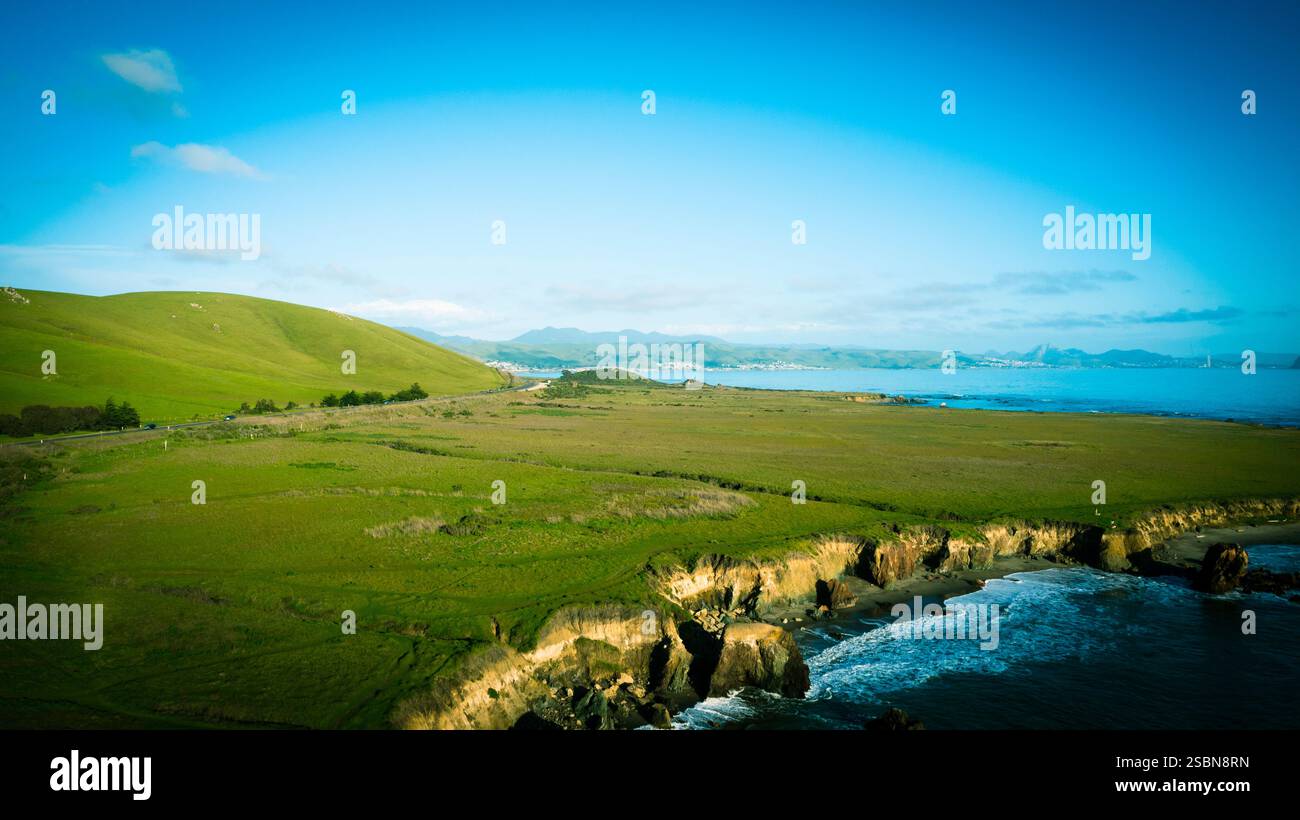 Green hills roll down to meet the shimmering ocean waves under a clear ...