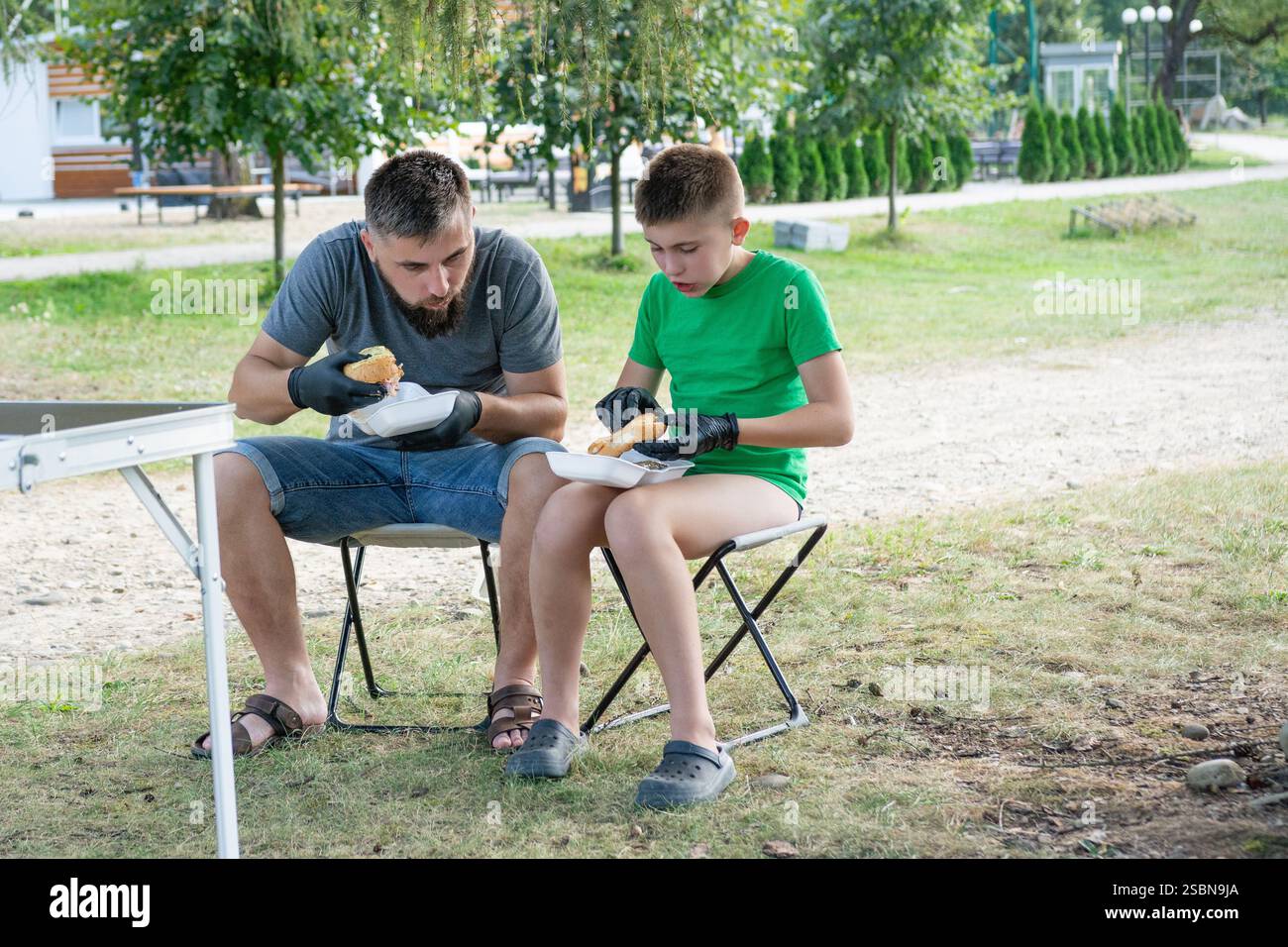 A man and boy sit at a small table outdoors, eating from disposable ...