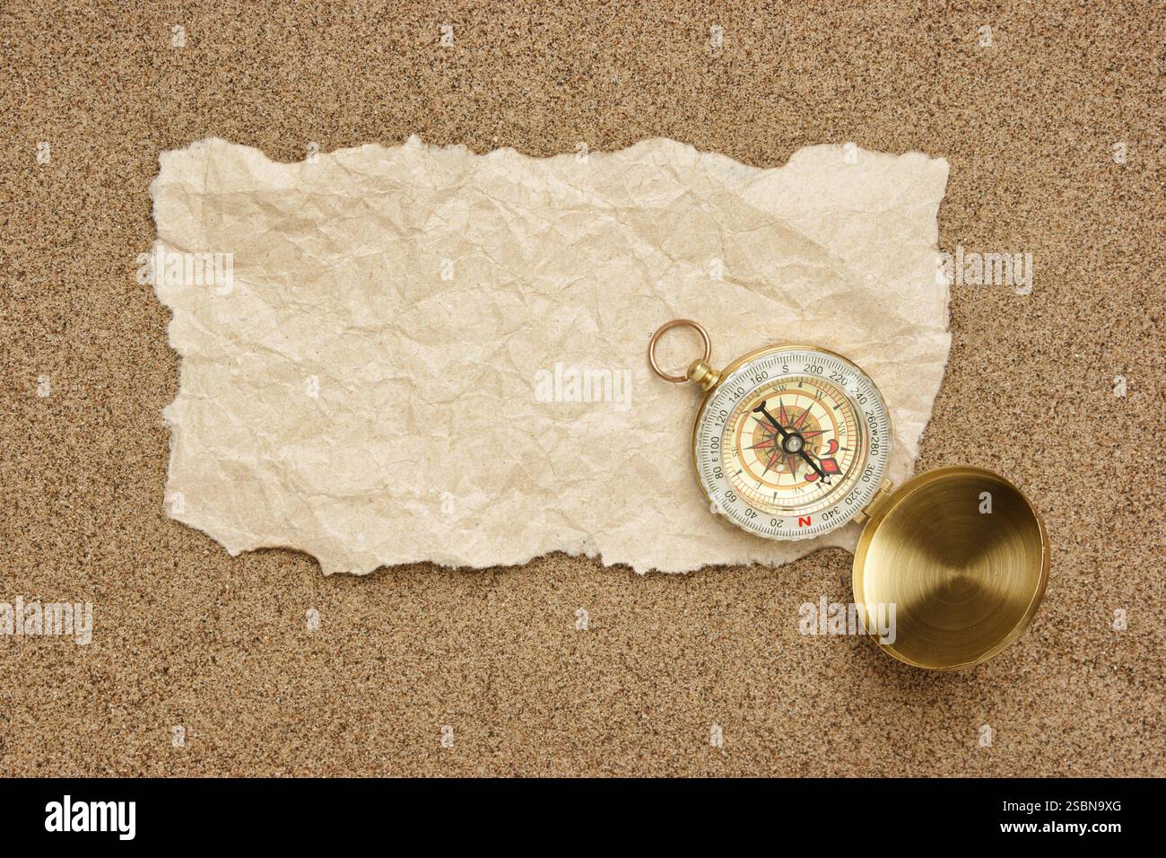 Compass on old sheet crumpled paper against the background of sand ...