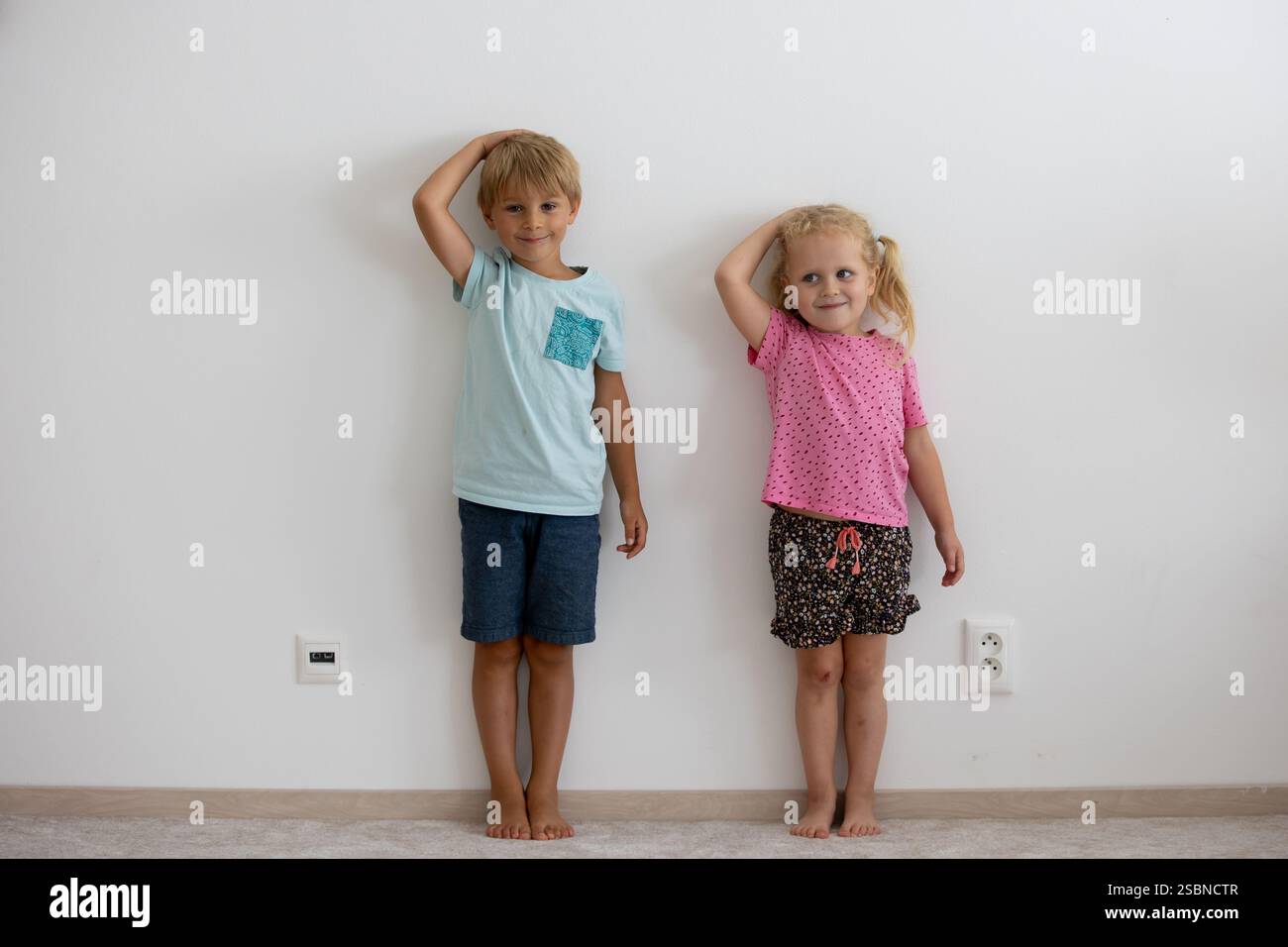 Little children, blond boy and girl, measuring height against wall in ...
