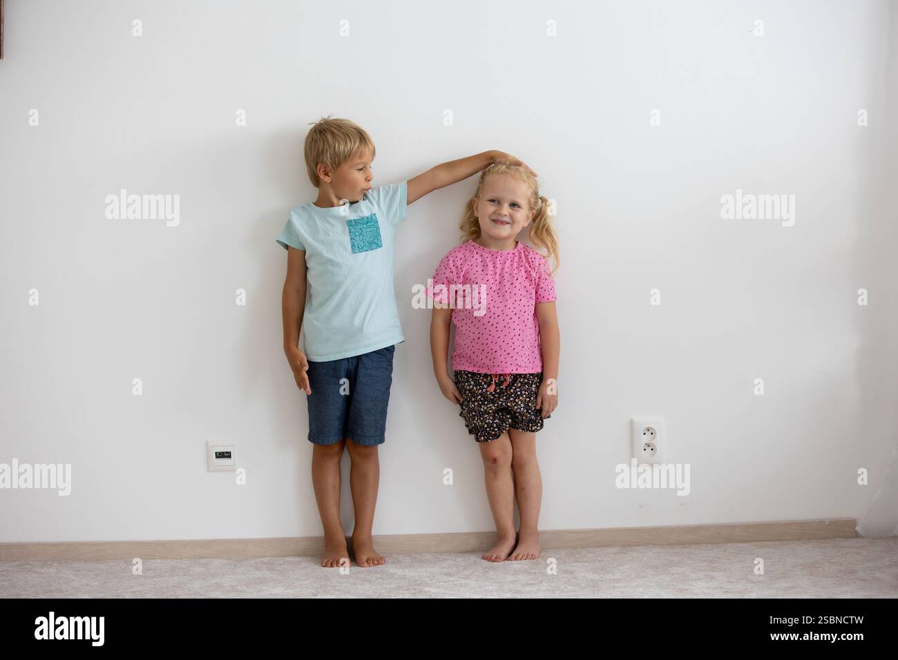 Little children, blond boy and girl, measuring height against wall in ...