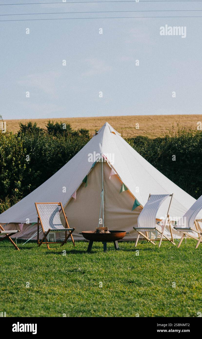 A white tent with a fire pit and two chairs in front of it. Scene is ...
