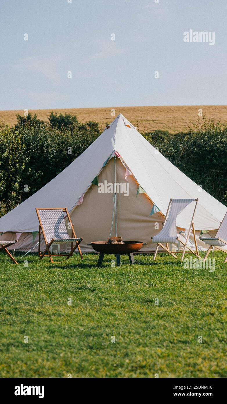 A white tent with a fire pit and two chairs in front of it. Scene is ...