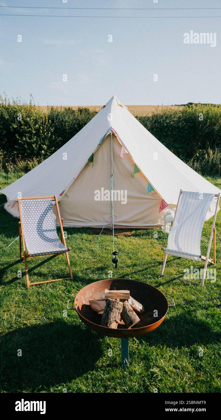 A white tent with a fire pit and two chairs in front of it. Scene is ...